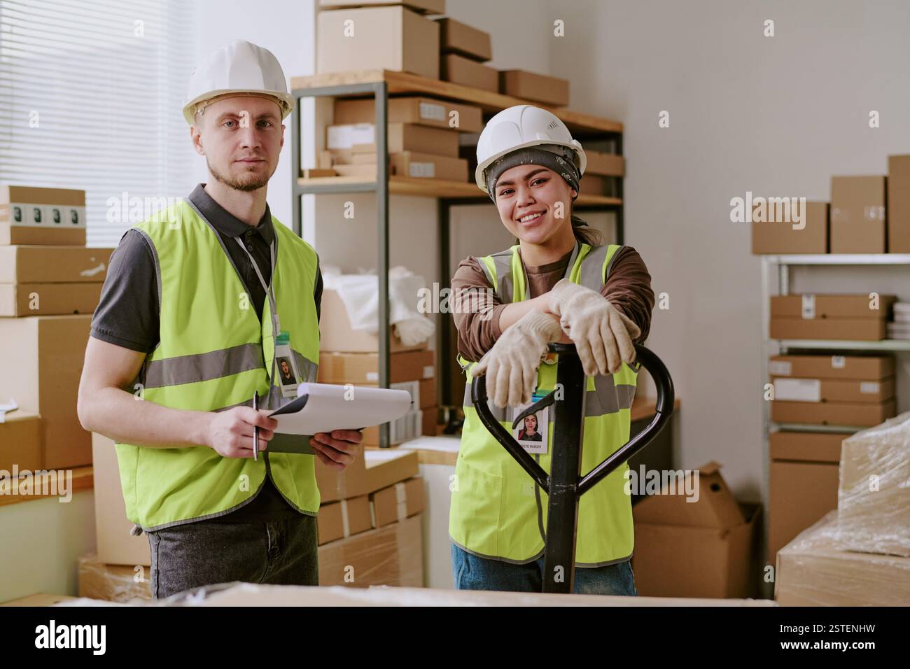 Portrait of two warehouse workers wearing helmets and safety vests ...