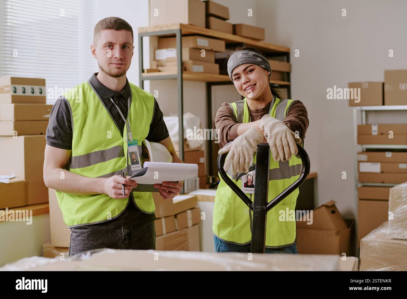 Two warehouse workers smiling while holding equipment and paperwork ...
