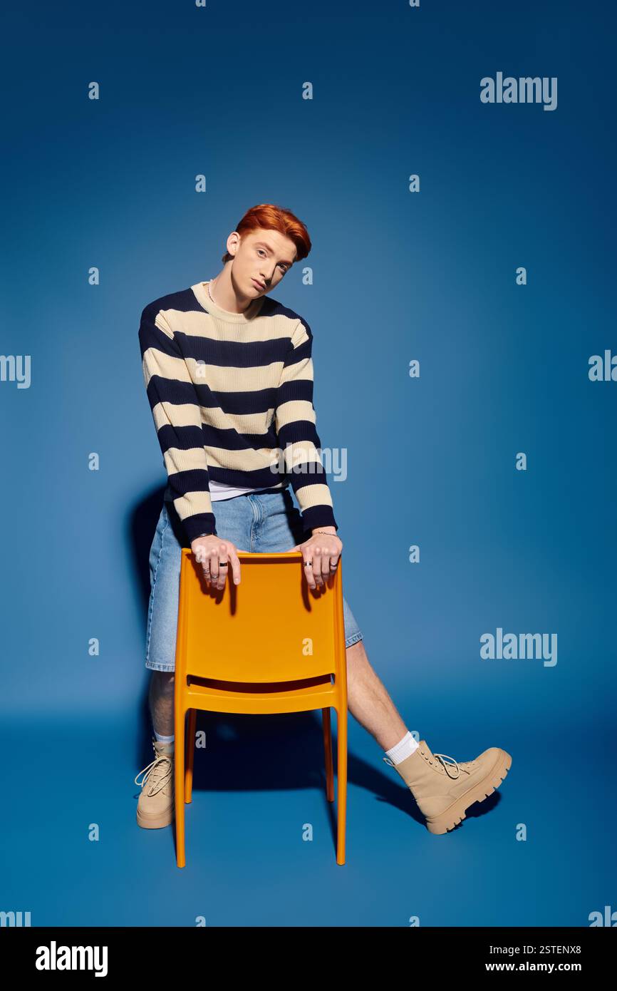 Emotional young man with striking features leans over a colorful chair ...