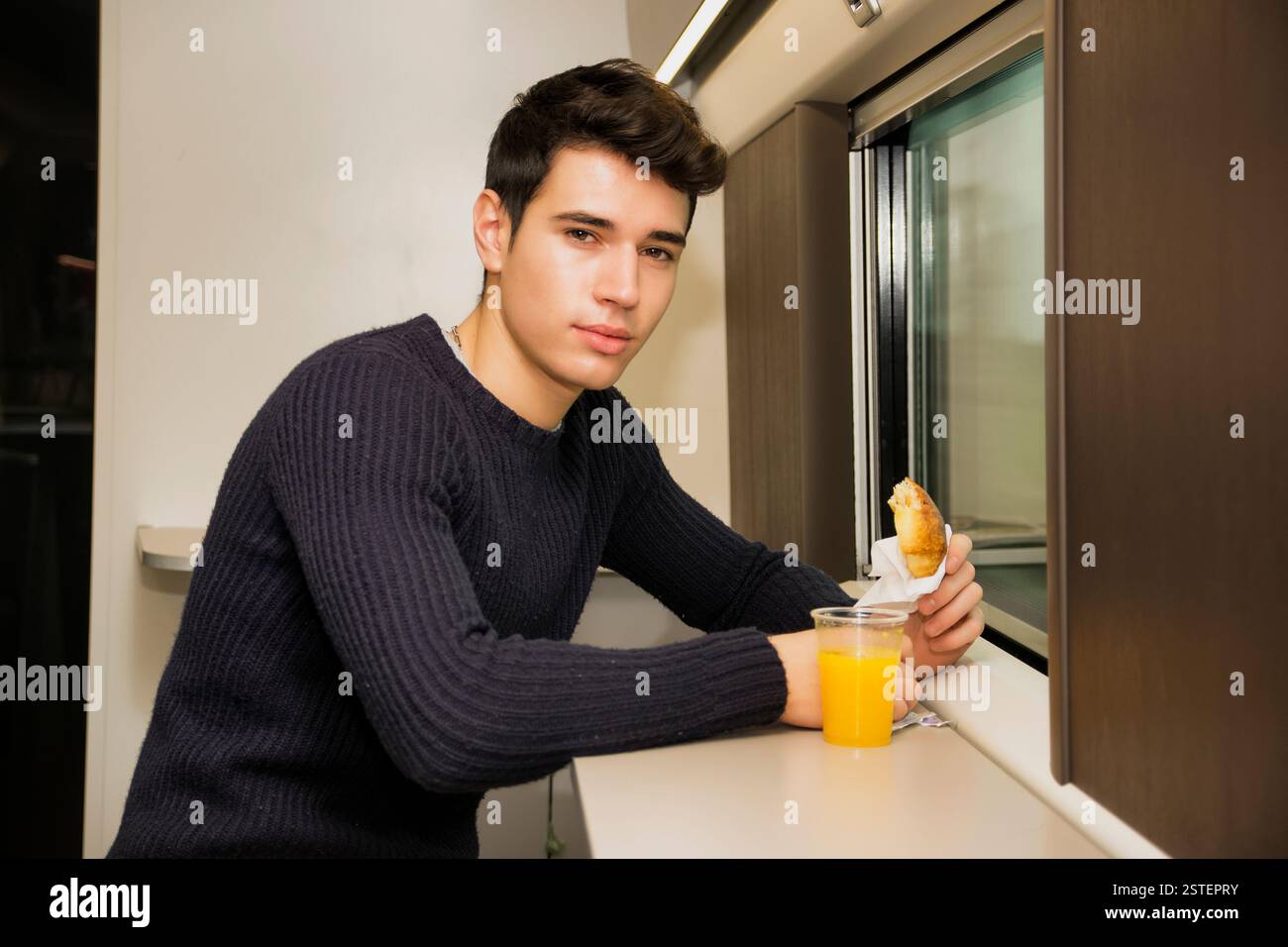 Young man eating refreshments on a train looking at camera while ...