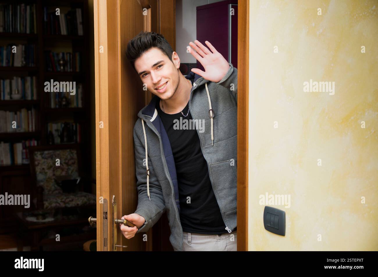 Smiling young man getting out of door waving at the camera Stock Photo ...