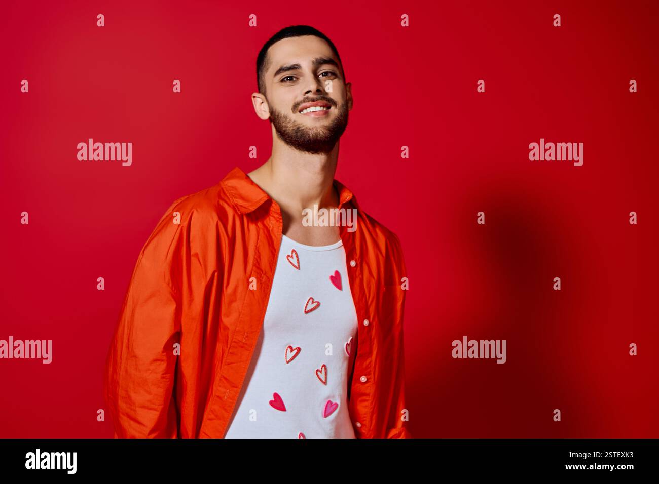 A charming young man stands confidently in a red backdrop, showcasing a ...