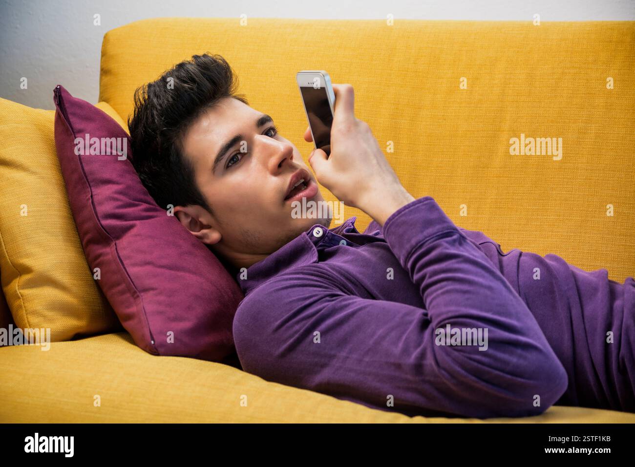 Attractive young man recording voice message on cell phone while laying ...
