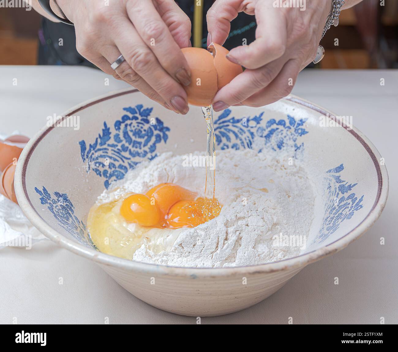 Cracking en egg with your hands and pouring it over flour in a ceramic ...