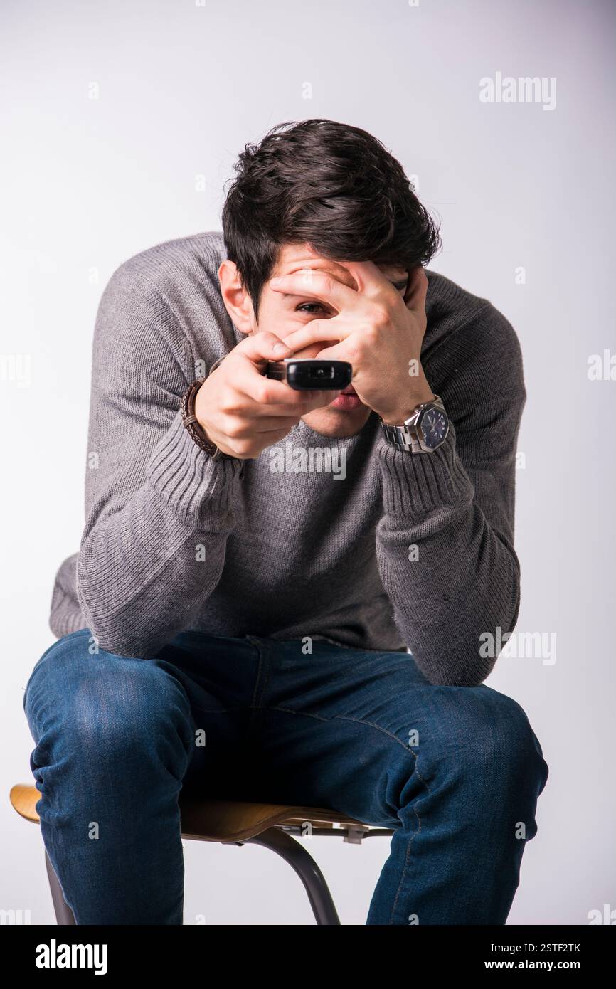 Handsome young man holding remote control and changing tv channels hi ...
