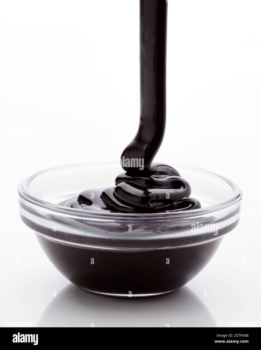 A thick black substance cascades into a clear glass bowl, forming soft ...