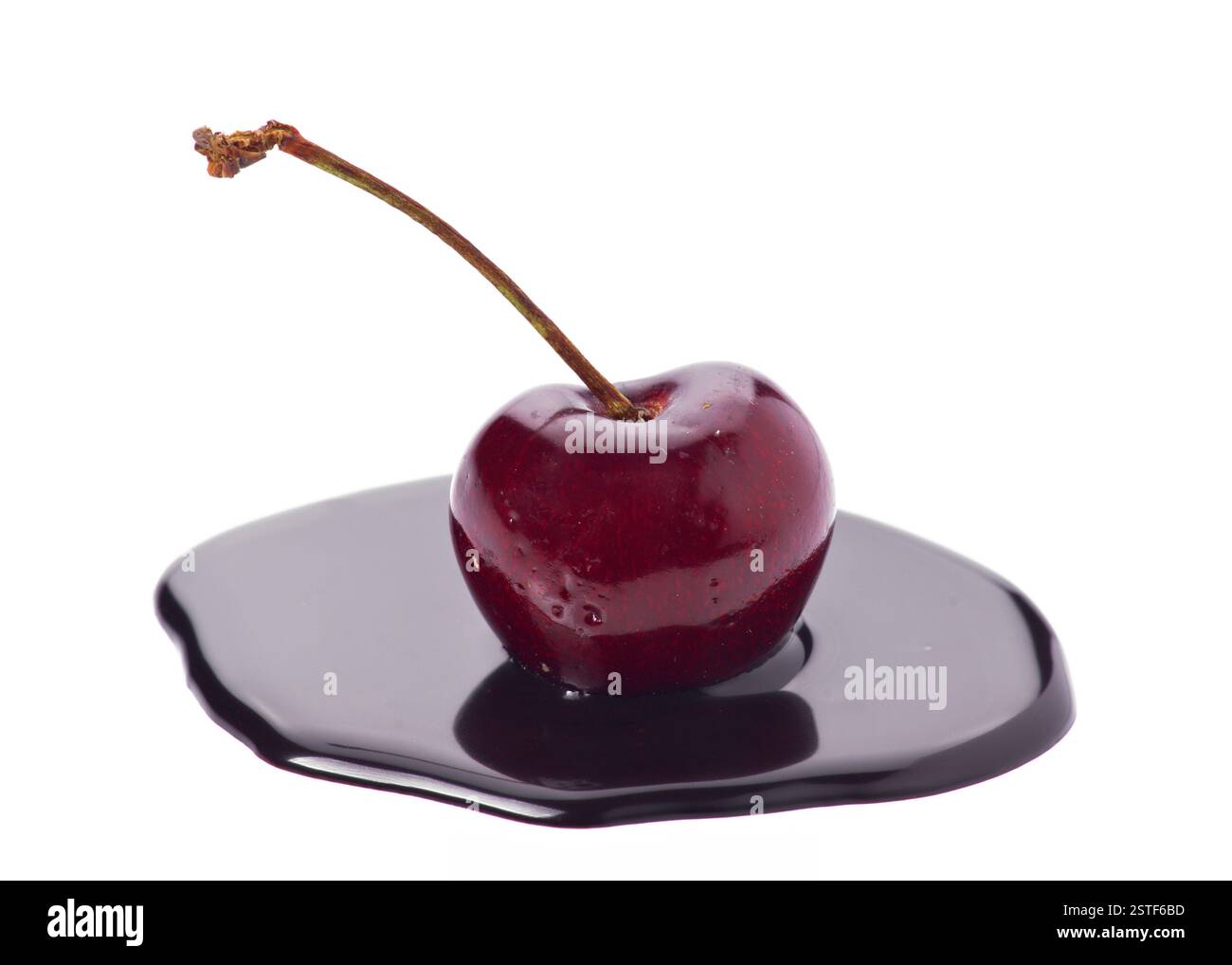 A bright red cherry sits atop a glossy black syrup puddle, showcasing ...