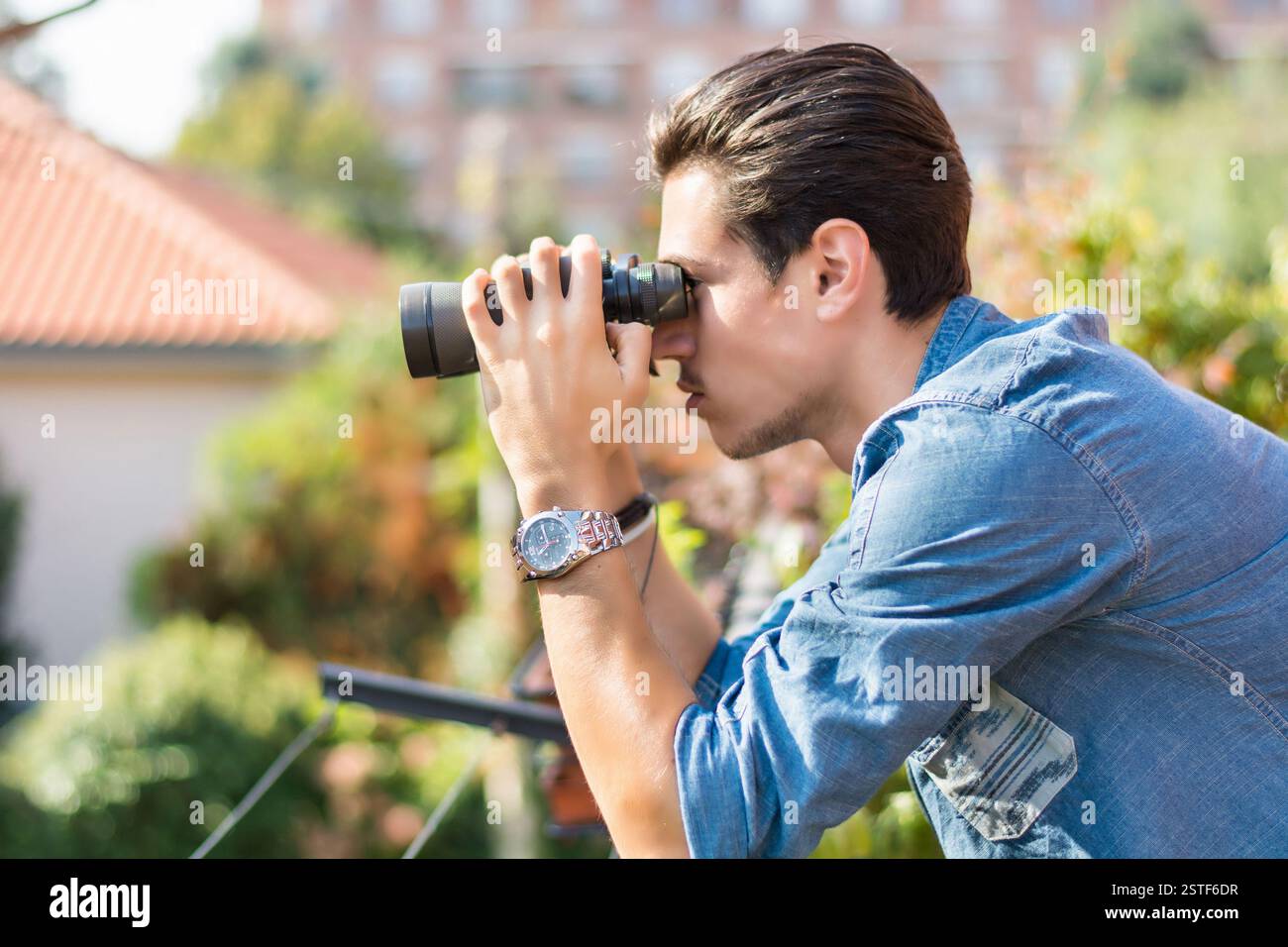 Young man looking through binocular searching outside from balcony hi ...