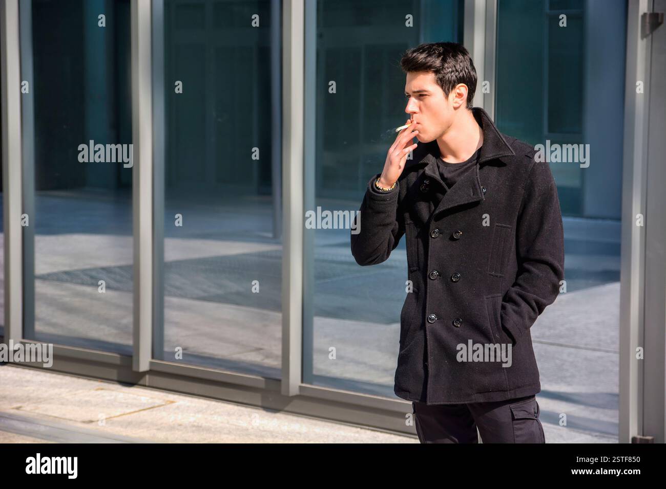 Handsome stylish young man smoking outside in urban setting Stock Photo ...