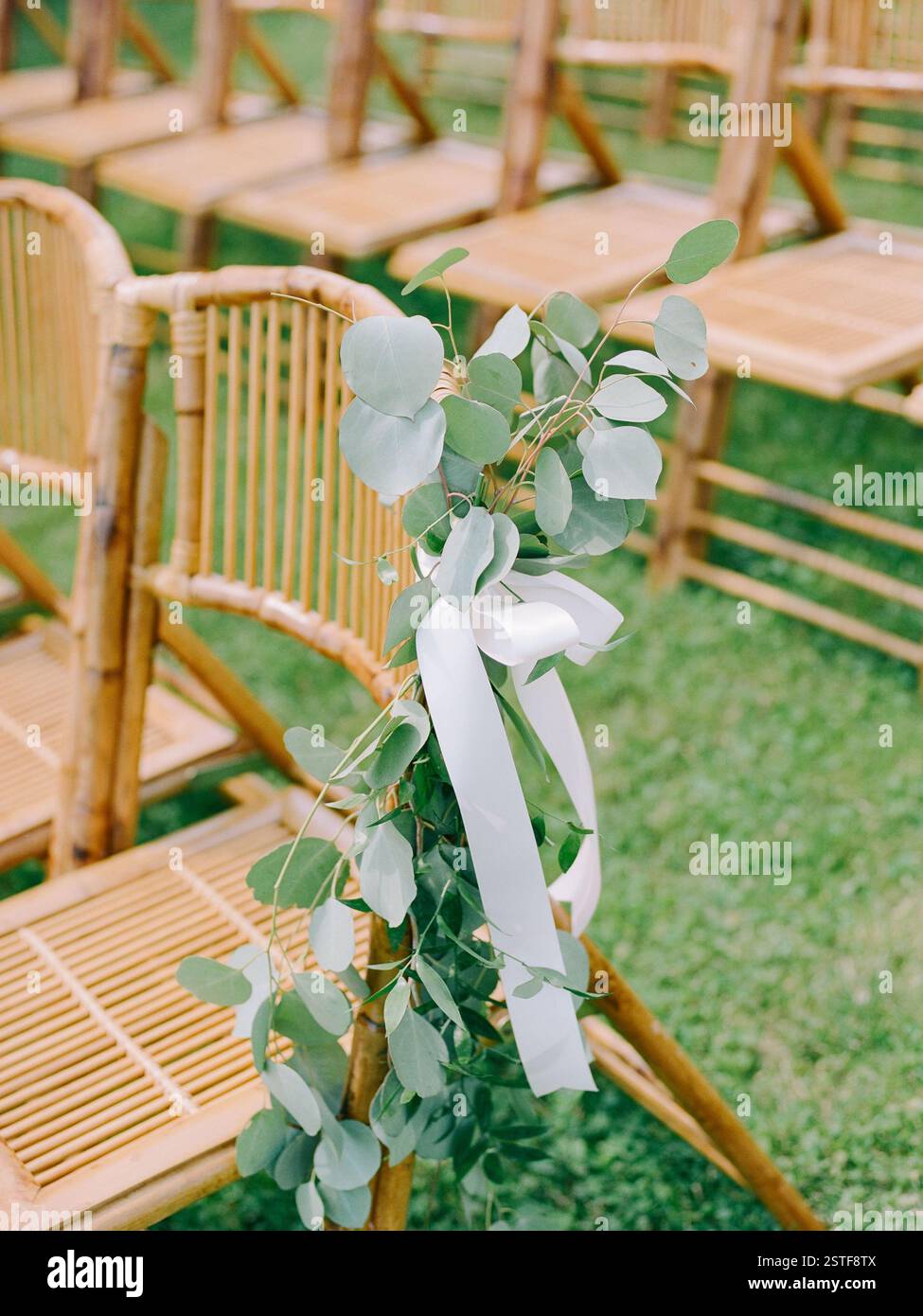 Greenery and a white ribbon decorate bamboo chairs set up for an ...