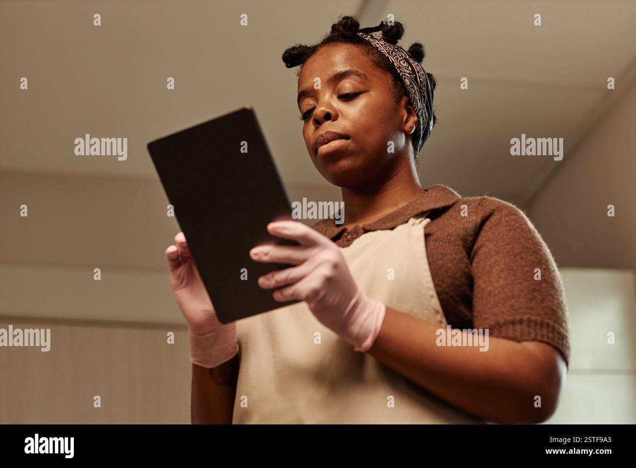 Chest up shot of adult Black female chef in apron using digital tablet ...