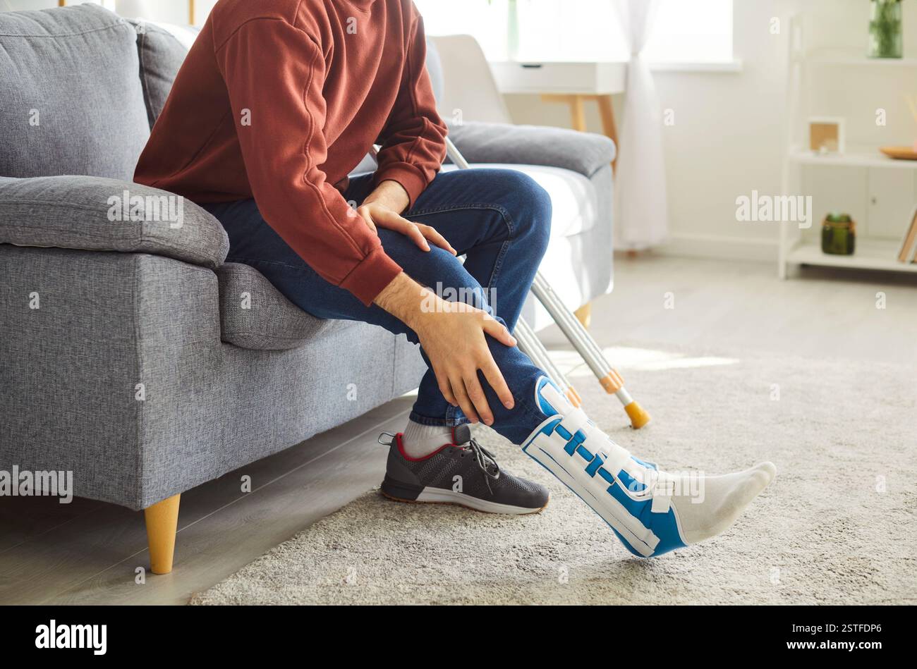 Man with leg in cast with crutch sitting on sofa at home after having ...