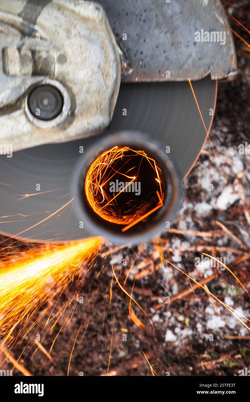 A close-up of a metal pipe being cut using an angle grinder. Sparks fly ...