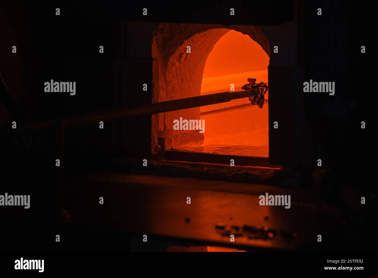 Molten glass on a blowpipe is inside of an open furnace, glass blowing ...