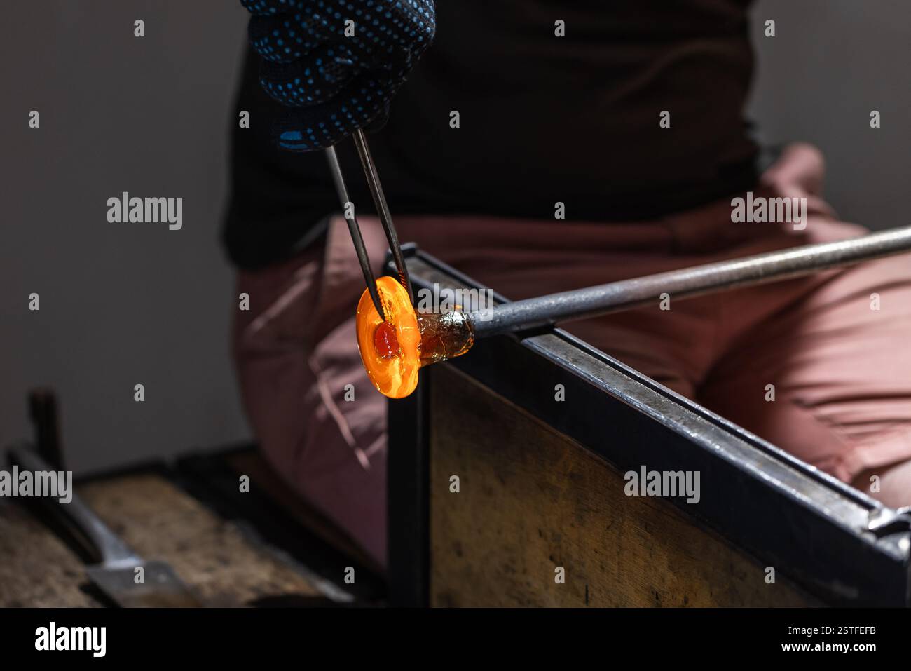 Molding red molten glass into a flower. Works of a glass blowing ...