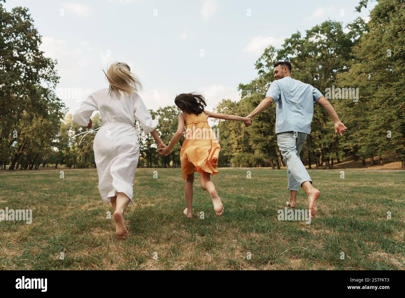 Happy family running together in a sunny green park outdoors Stock ...