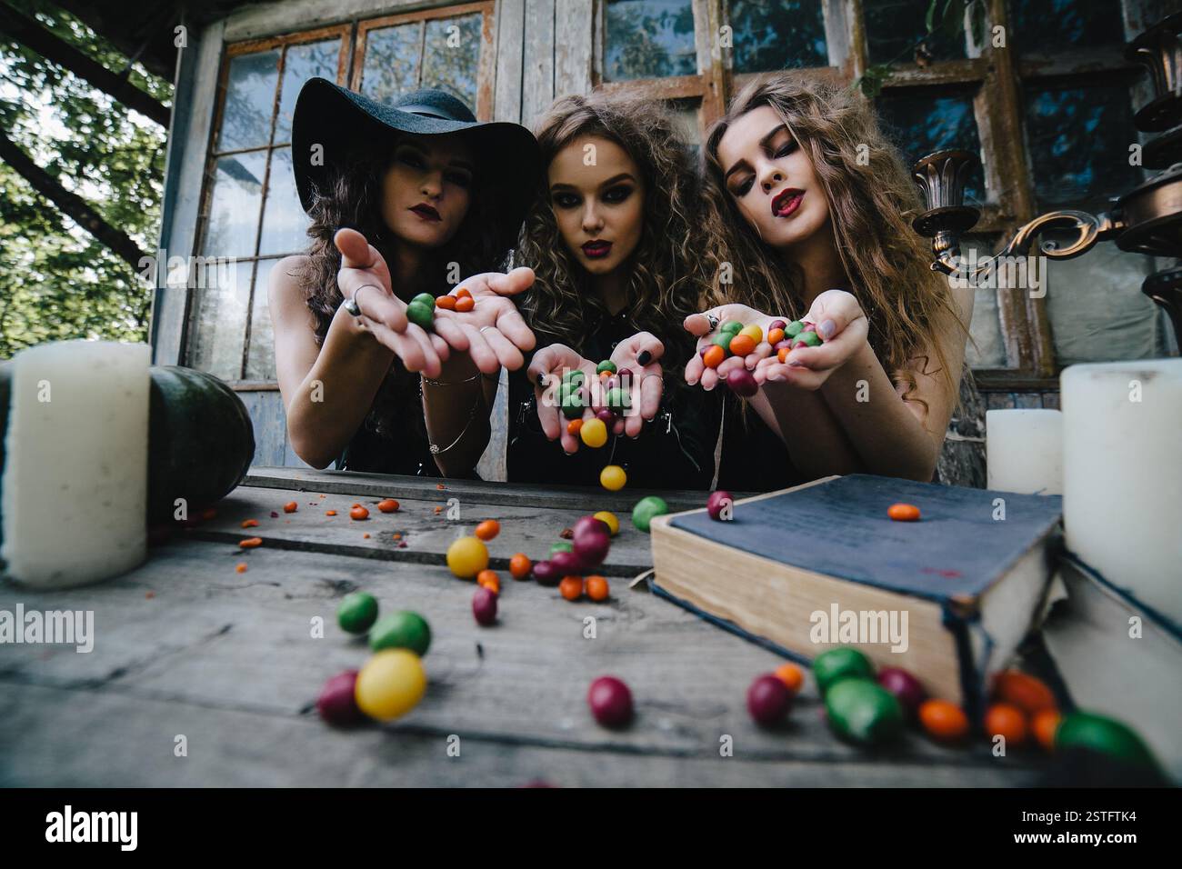 Three vintage witches perform magic ritual, throwing sweet at a table ...