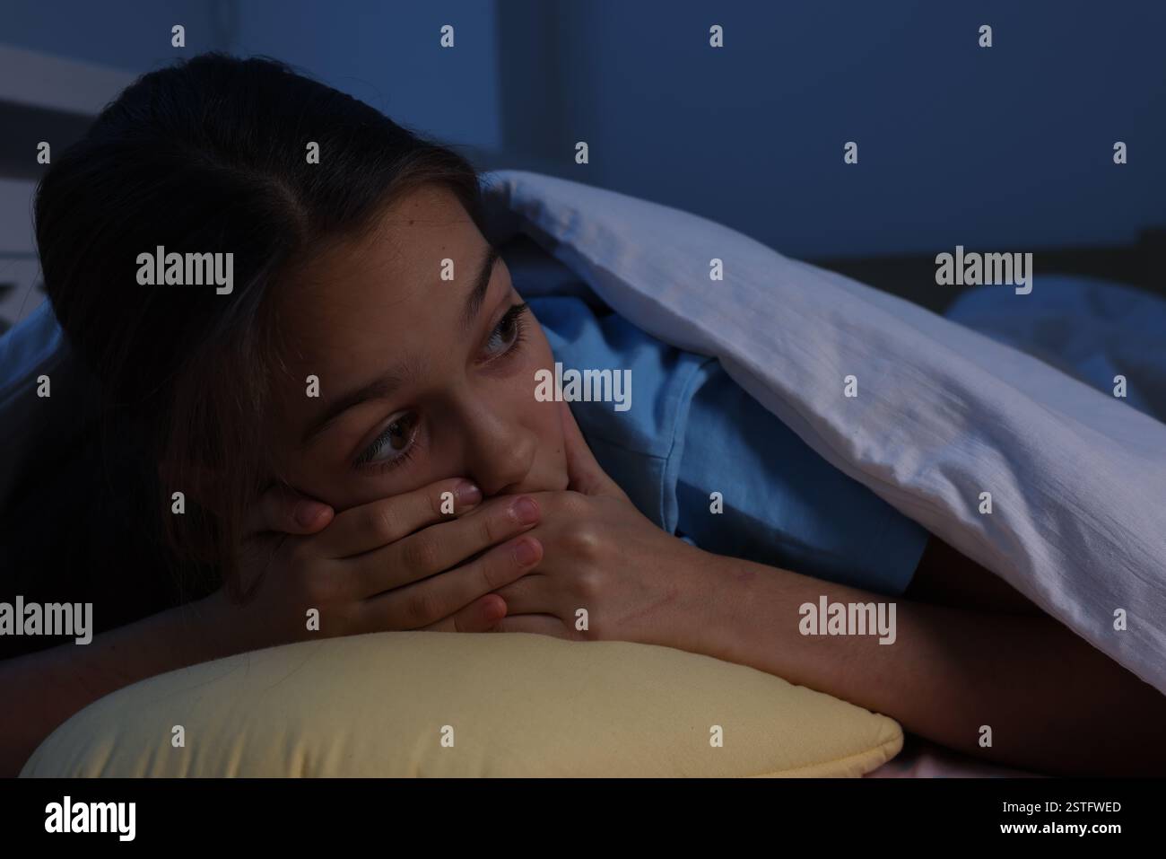 Afraid girl with pillow under duvet on bed at night Stock Photo - Alamy