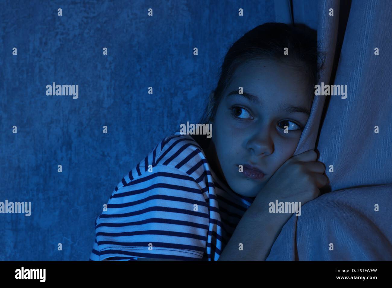 Scared girl hiding behind curtain at night. Space for text Stock Photo ...