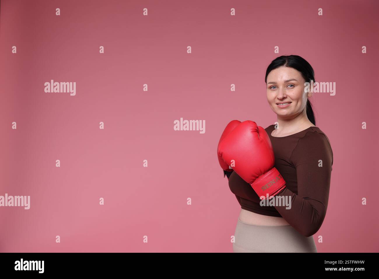 Plus size woman in gym clothes with boxing gloves on pink background ...