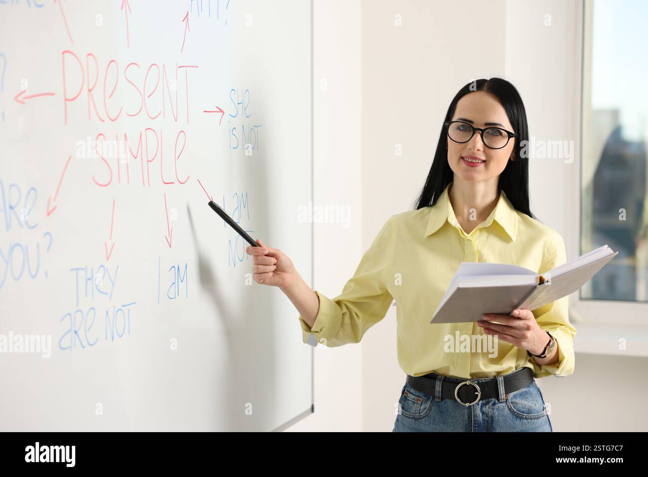 English teacher explaining Present Simple tense at whiteboard in ...