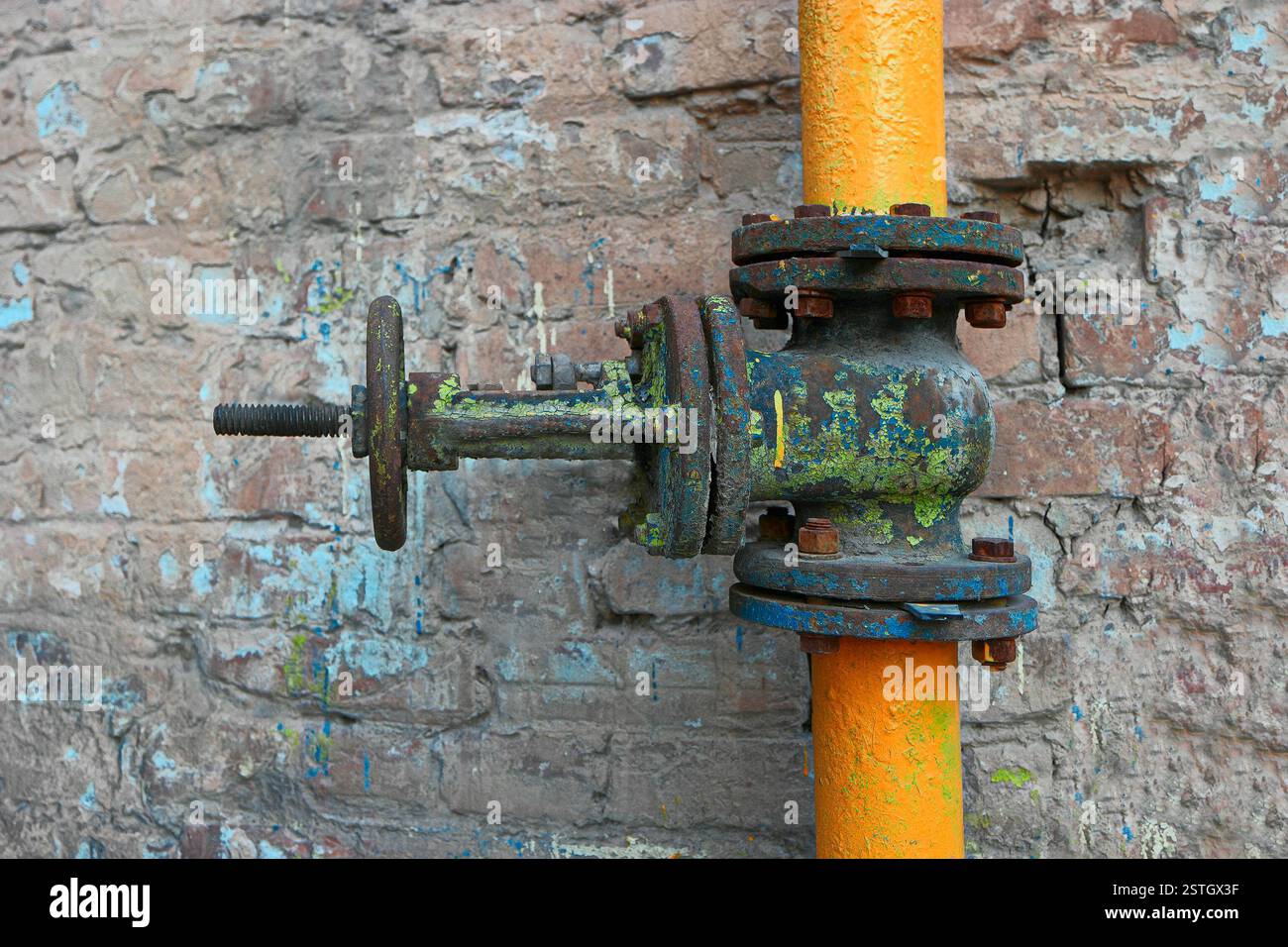 Old dusty and rusty valve and pipes of yellow color on weathered brick ...