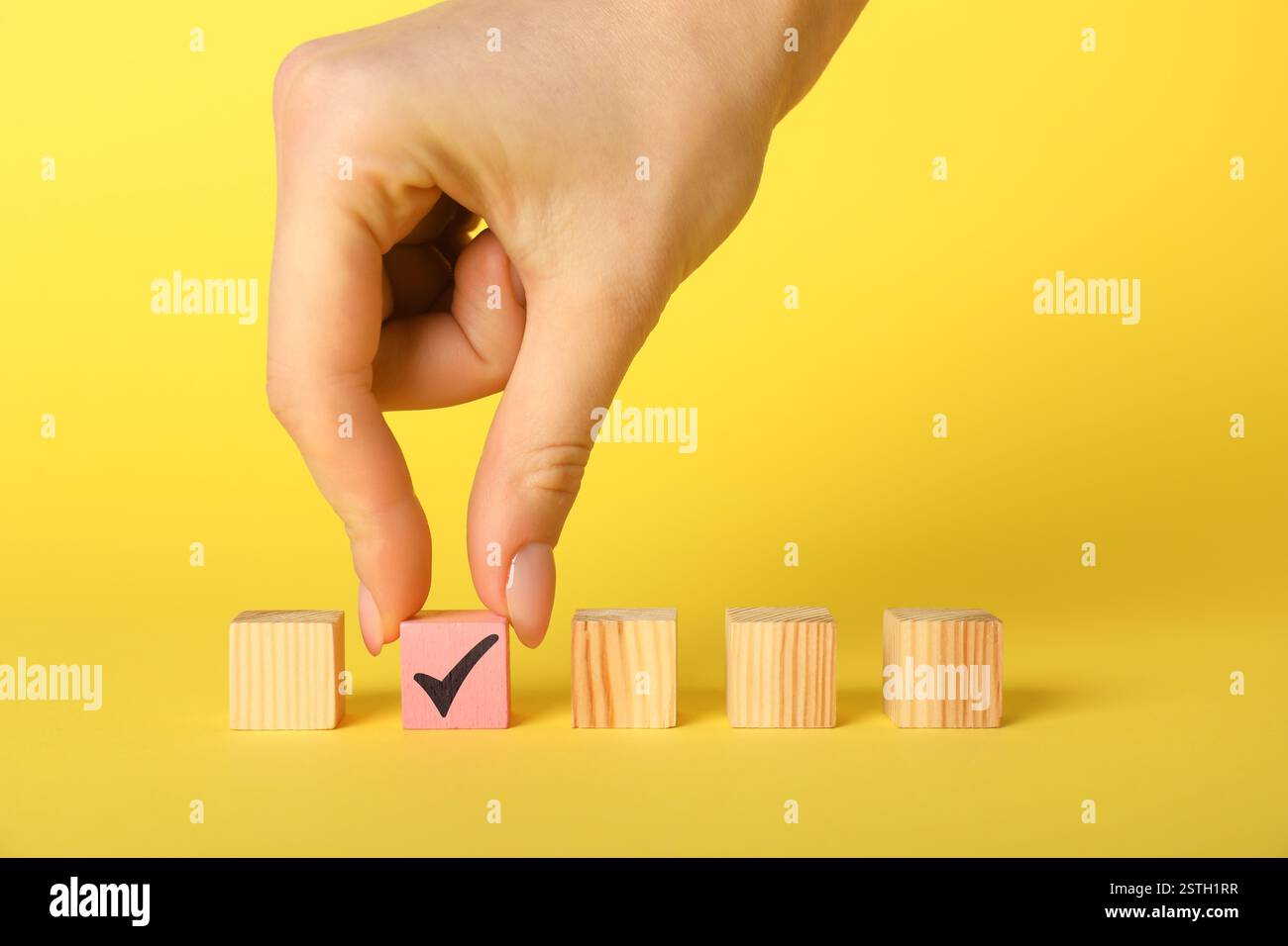 Woman taking pink cube with check mark on yellow background, closeup ...