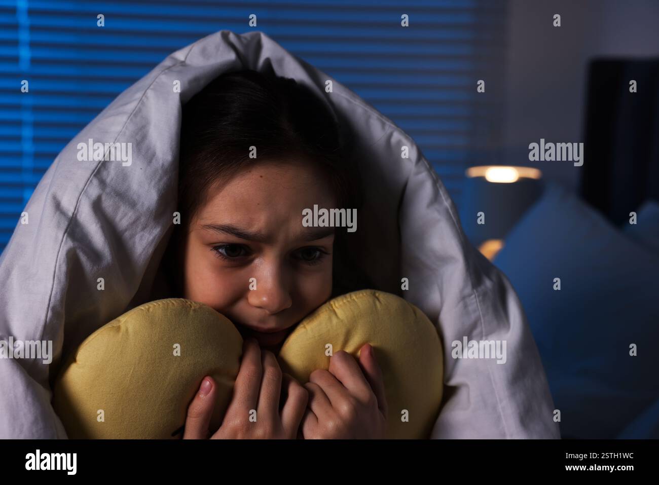 Afraid girl with pillow under duvet on bed at night Stock Photo - Alamy