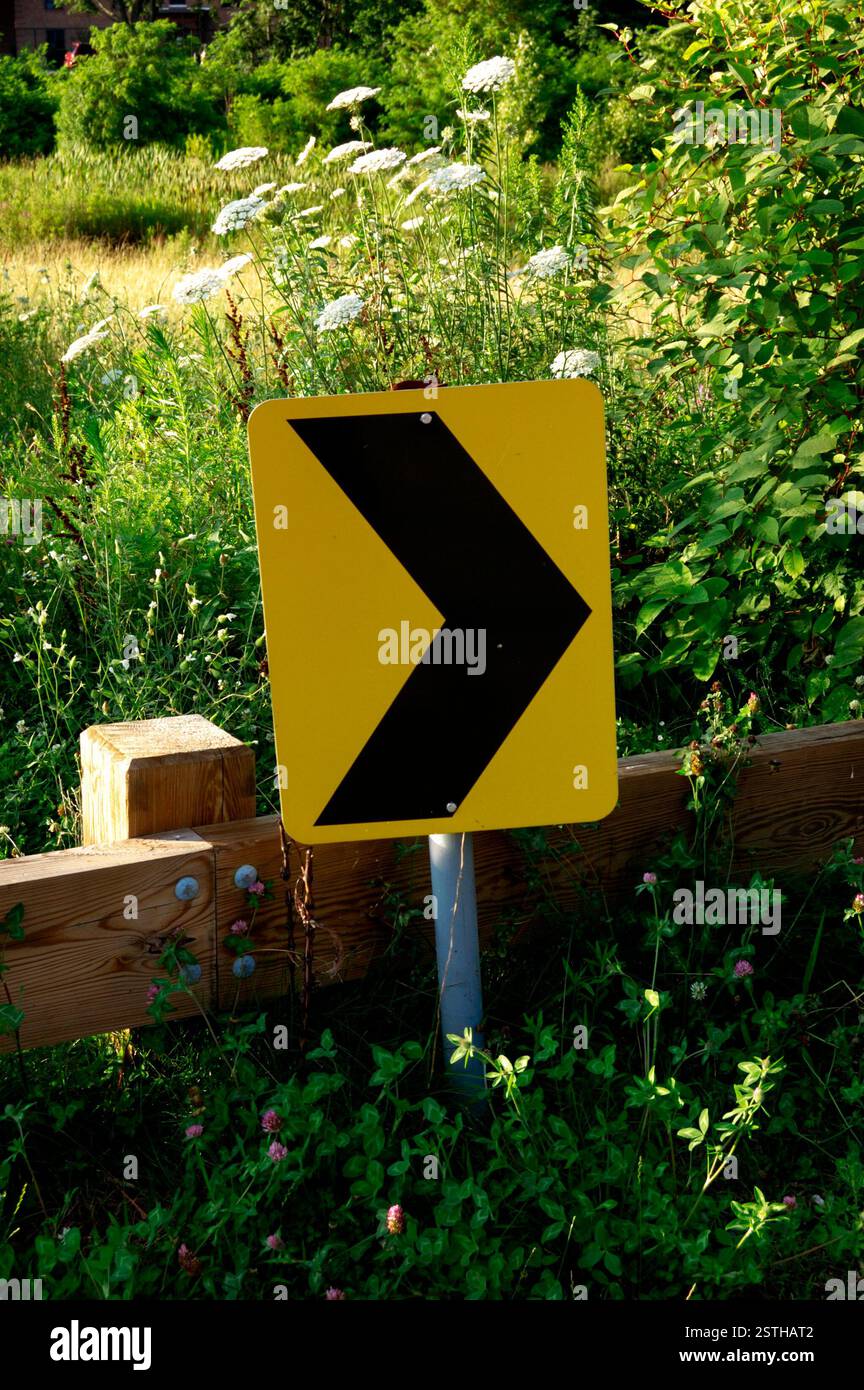 Road sign indicating direction on curved road in front of wooden fence ...
