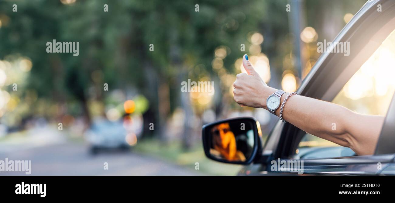A female driver puts her hand out the car window while driving and ...