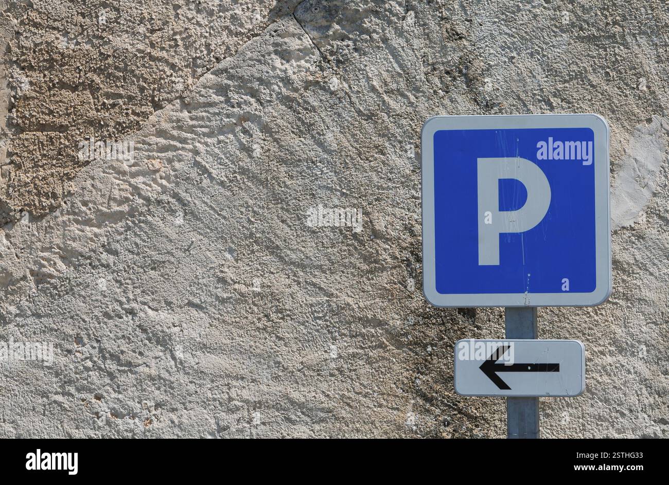 A blue car park sign with a white arrow on a rough, textured wall ...