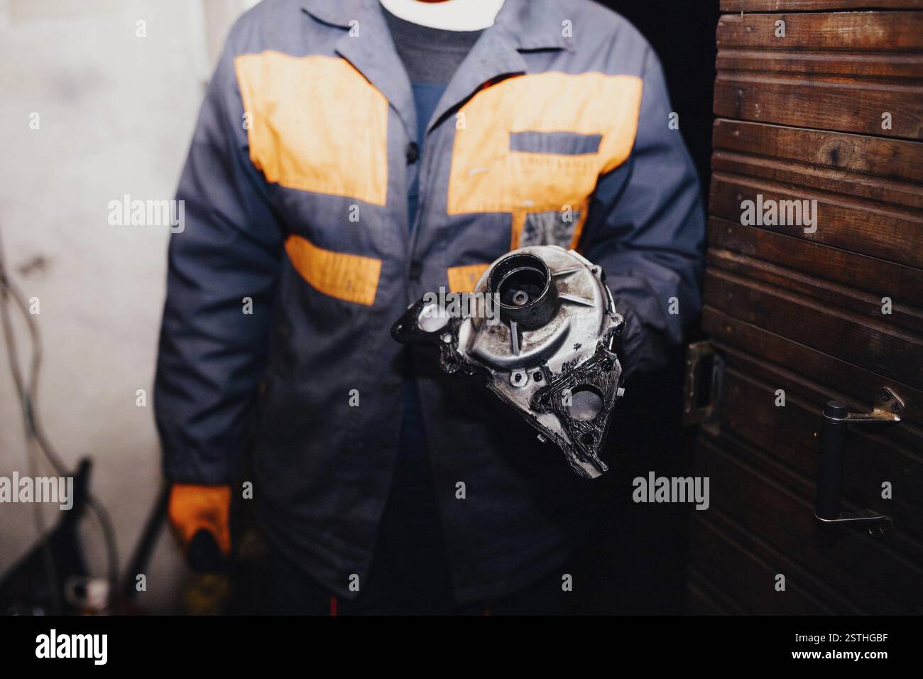 Mechanic wearing blue and orange uniform holds an engine part inside a ...
