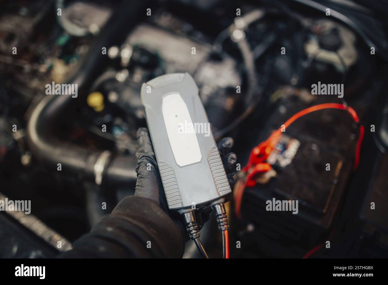 A gloved hand holds a diagnostic tool with cables attached in a car ...