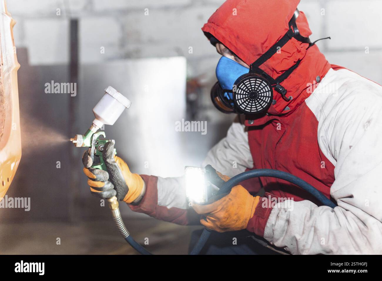 A person in protective gear using a spray gun, illuminating the work ...
