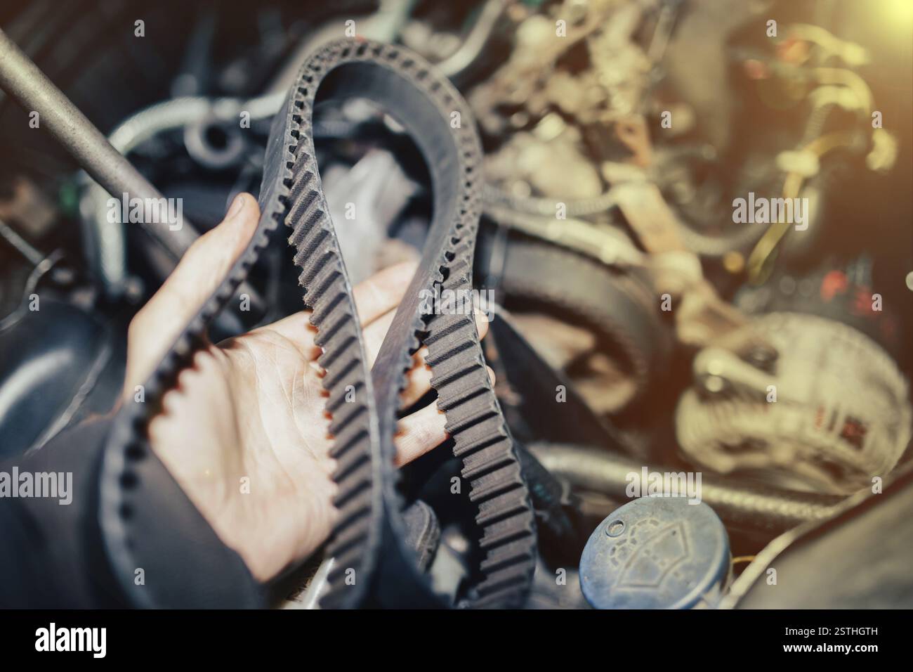 Hands holding a timing belt with sunlight illuminating a car engine bay ...