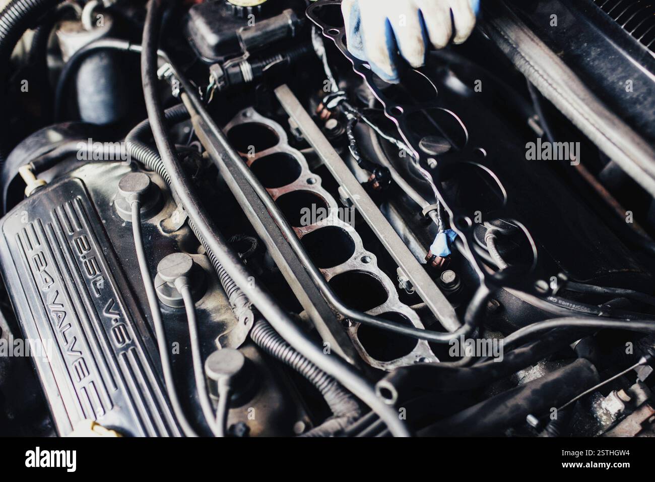 Mechanic working on a car engine with components and cables visible ...