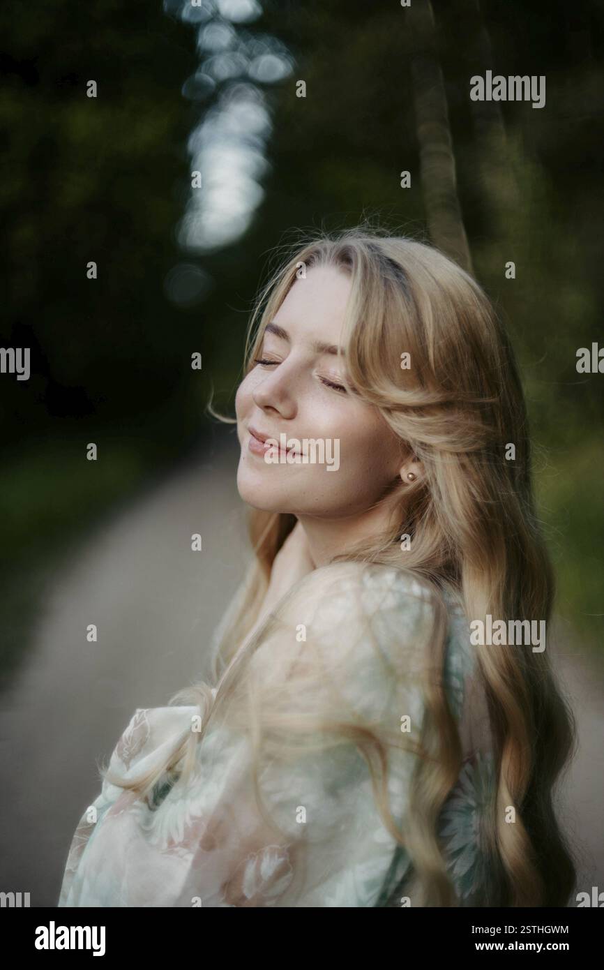 A serene image of a woman with closed eyes, standing on a path ...