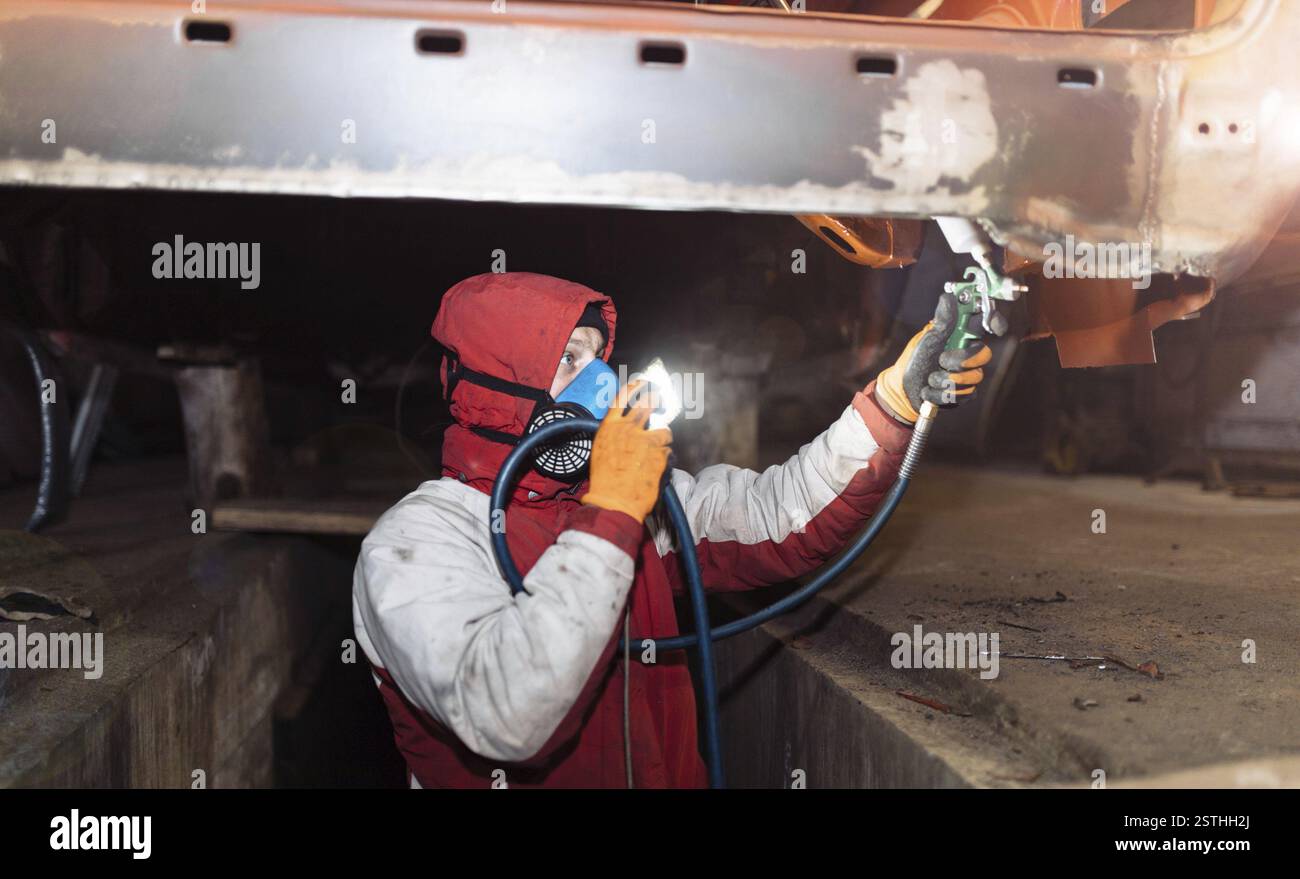 Individual applying anti-rust coating under a vehicle with a spray gun ...