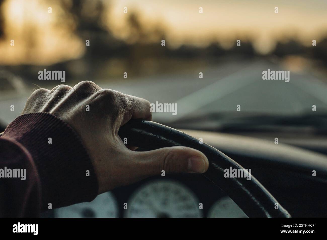 A person's hand grips a steering wheel while driving on a highway in ...