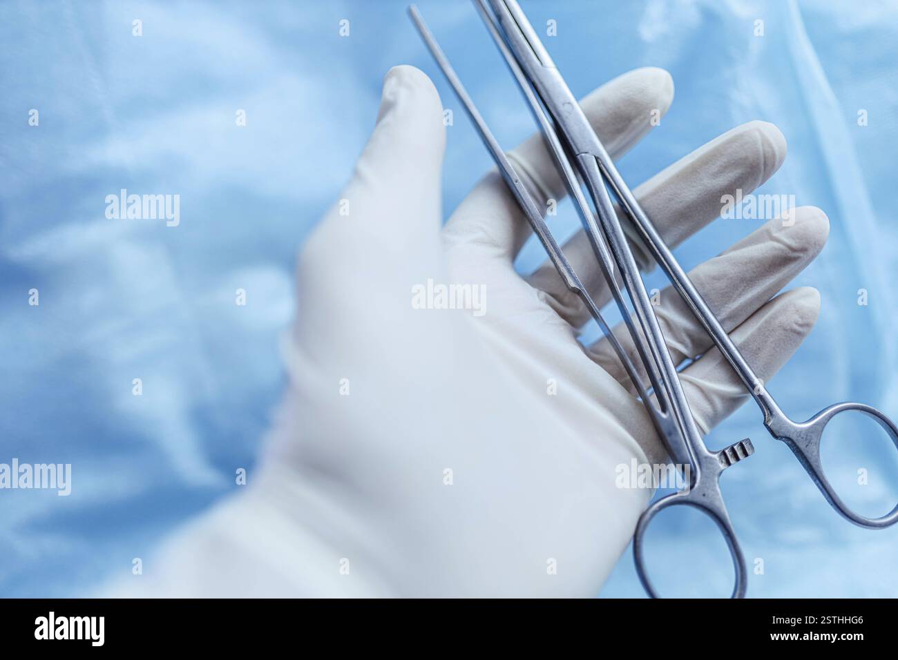 A hand in gloves holding surgical instruments on a blue sterile ...