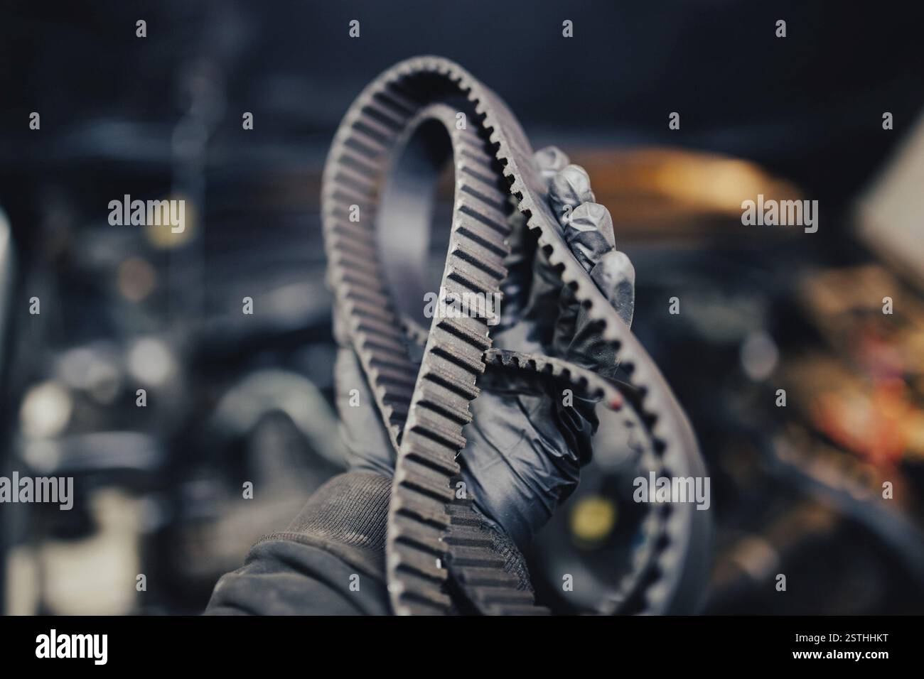 A person wearing gloves holds a timing belt in a car engine bay Stock ...
