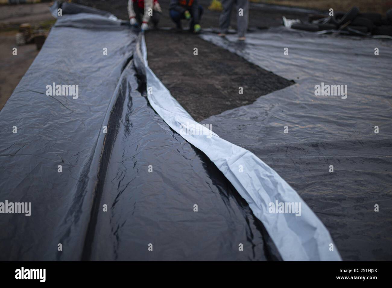 Black plastic tarp being spread out on the ground at a worksite Stock ...