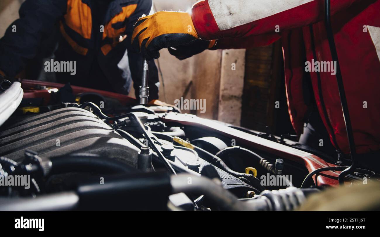 Mechanic wearing gloves works on a car engine in a dimly lit garage ...
