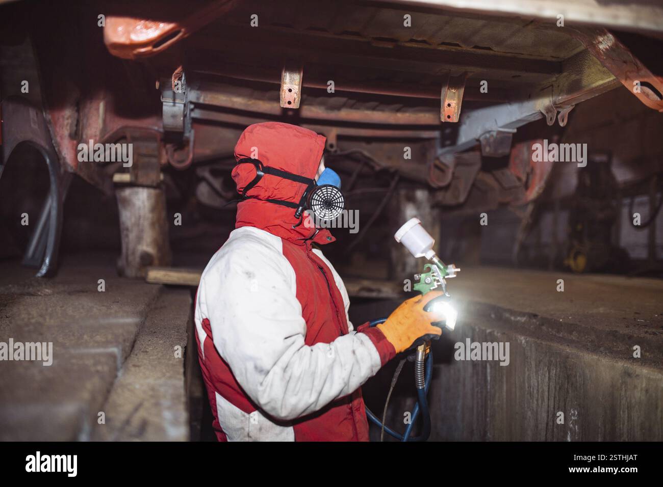 Mechanic in protective gear spray painting the underside of a vehicle ...