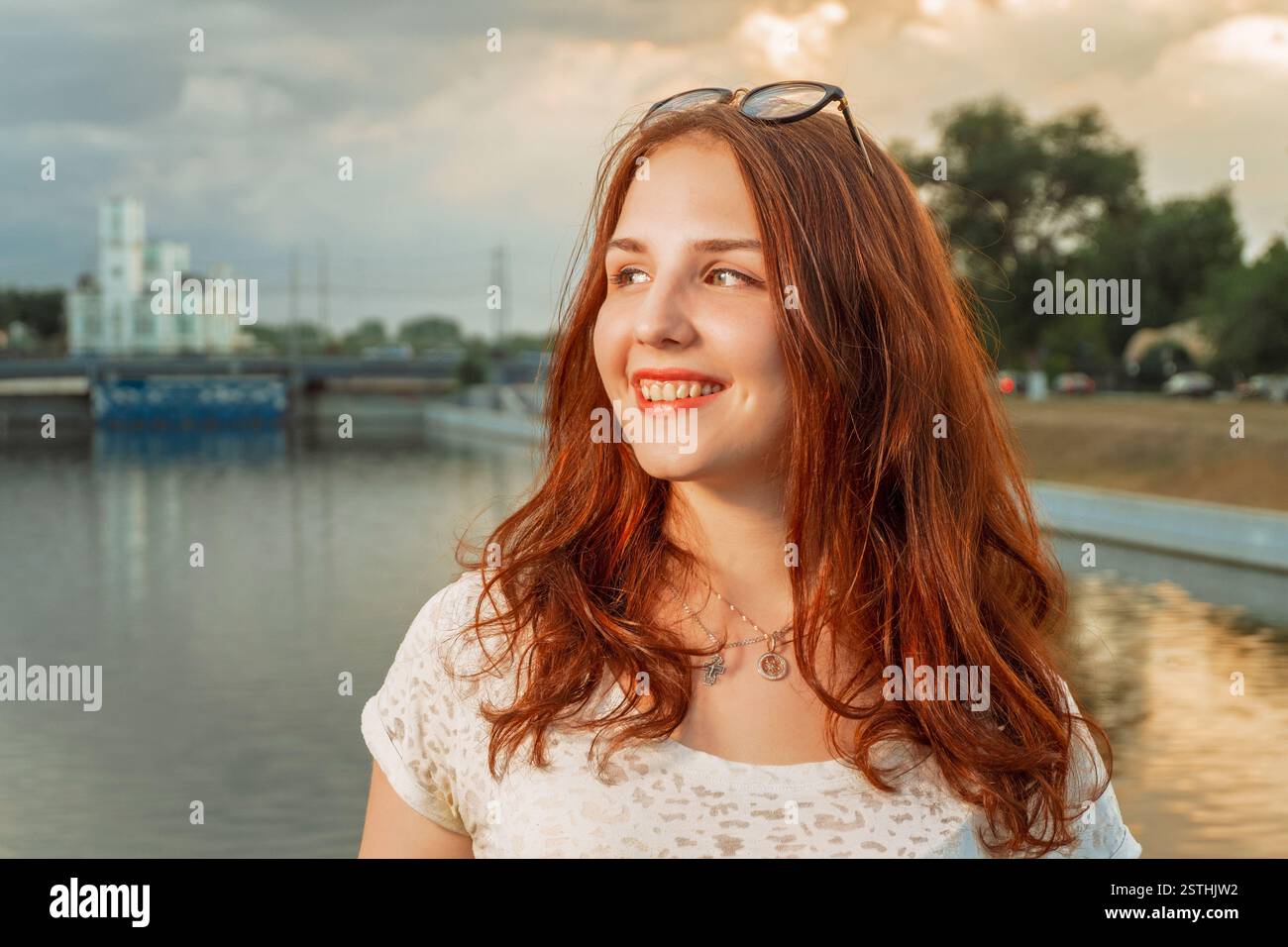Portrait of a smiling young red haired woman over city river landscape ...
