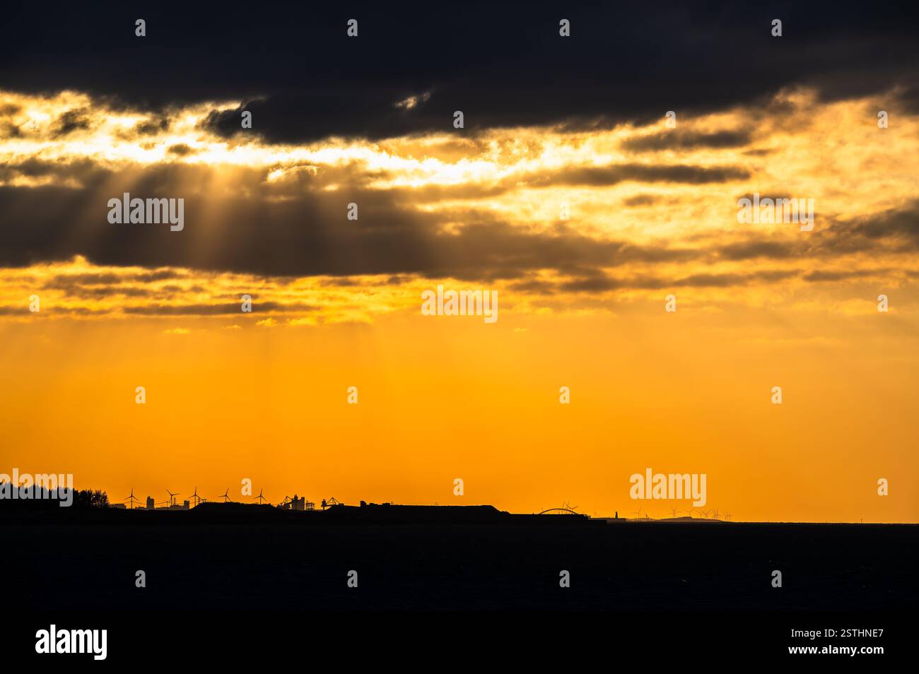 Sun rays pierce through dramatic clouds, illuminating wind turbines in ...