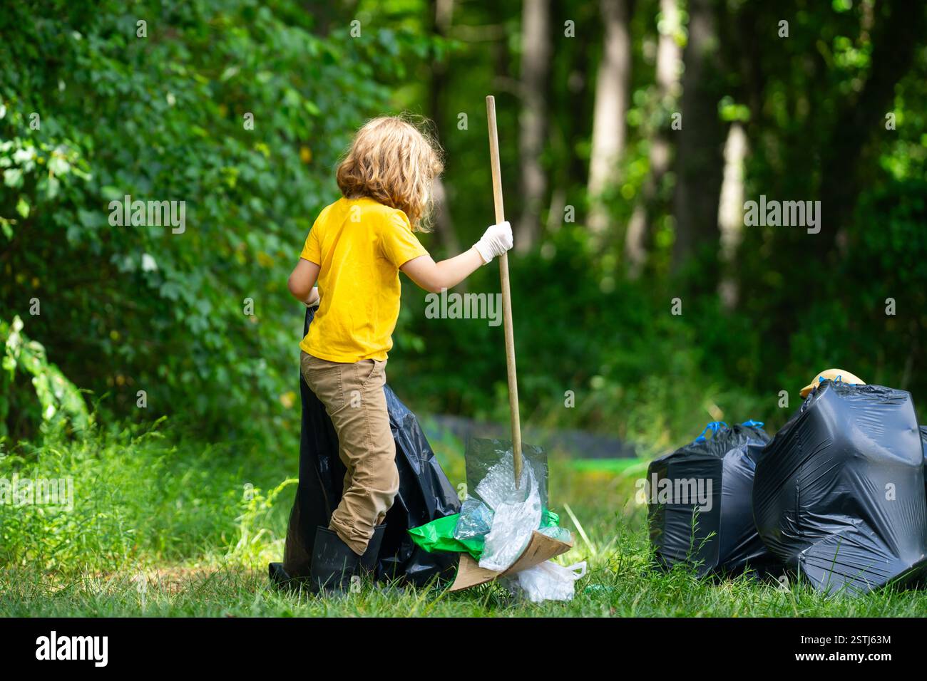 Kid cleaning up the park, putting trash in a garbage bag. Environmental ...