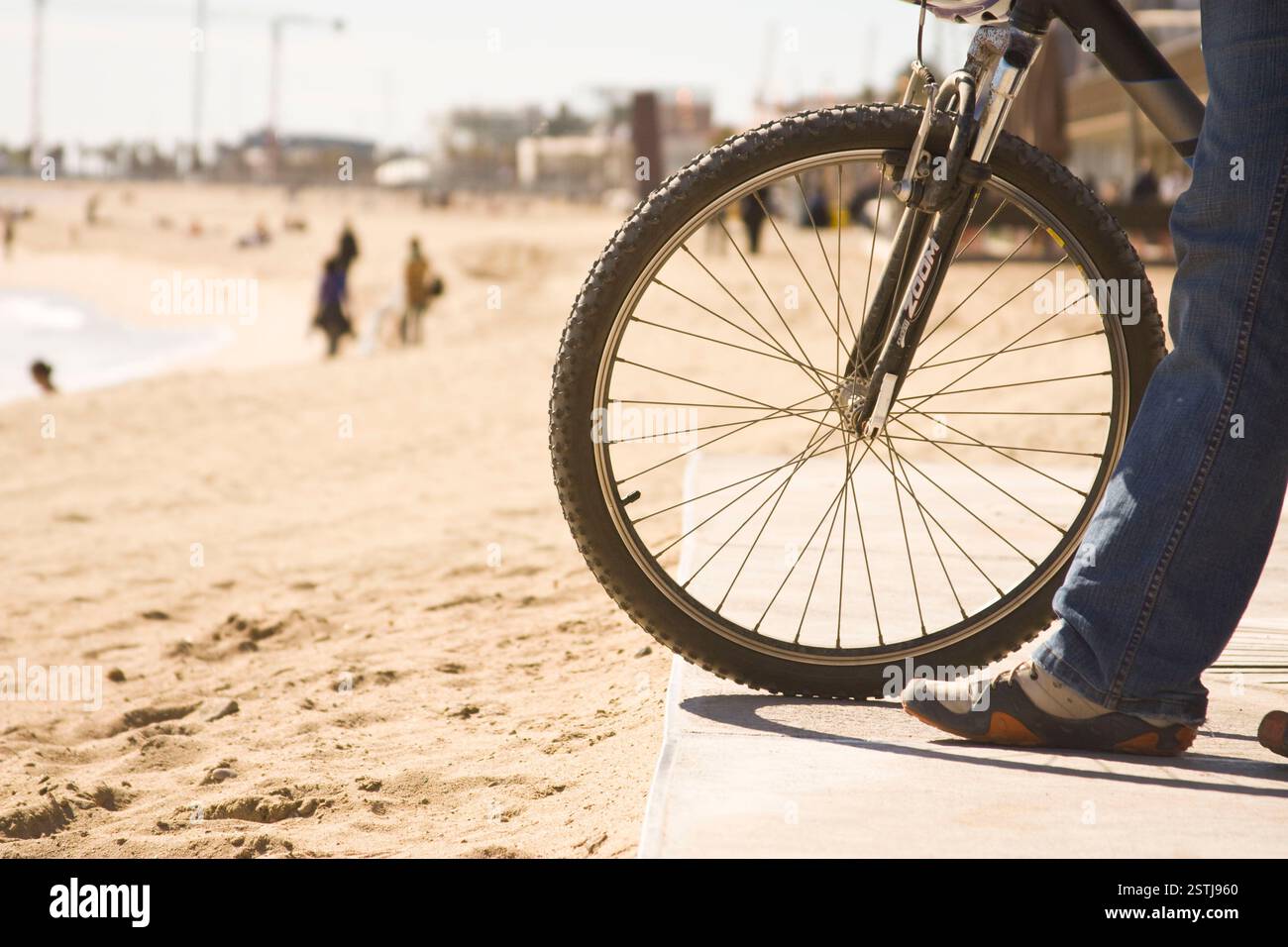 Bicycle wheel and rider's legs at a sandy beach. Personal perspective ...