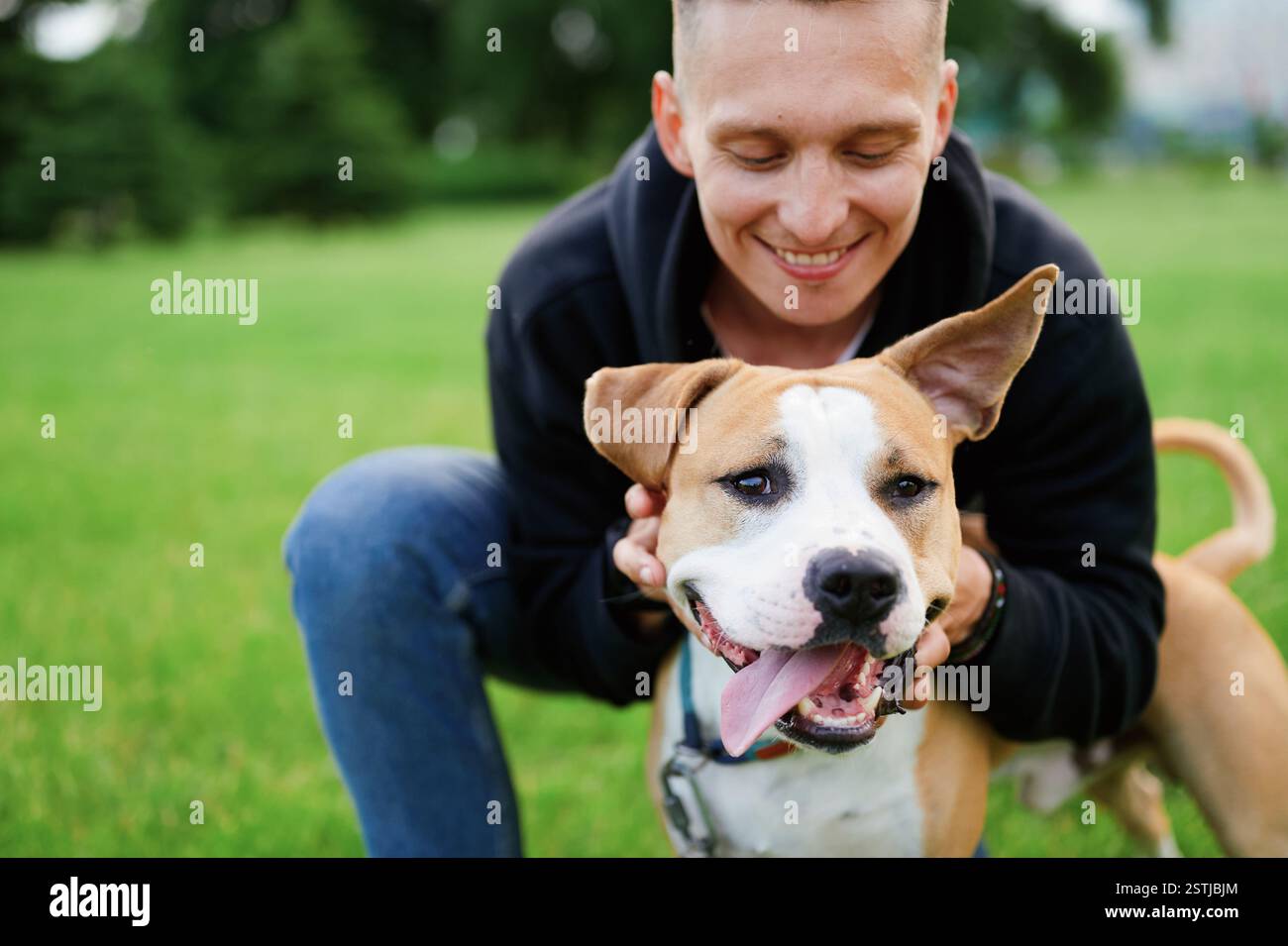 Young man sitting on the grass holding his puppy by the head. Dog ...