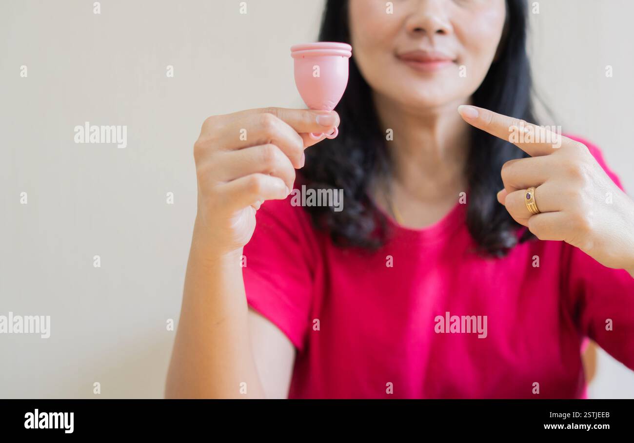 Happy Asian woman pointing at menstrual cup on light beige color ...